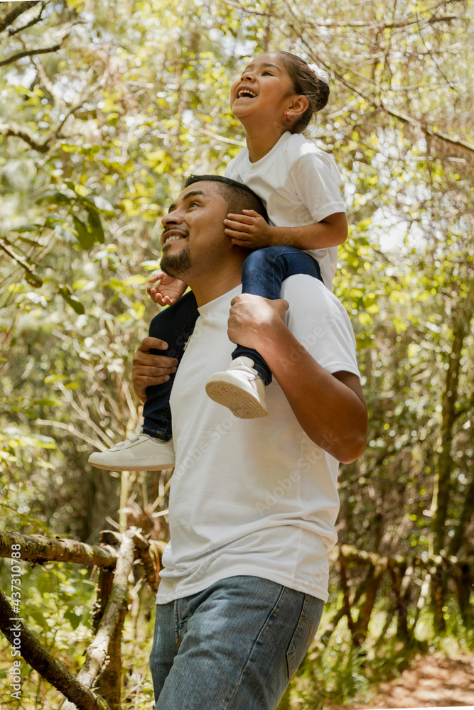 Hispanic dad carrying his daughter on his shoulders-Family walking in the park-Father playing ...