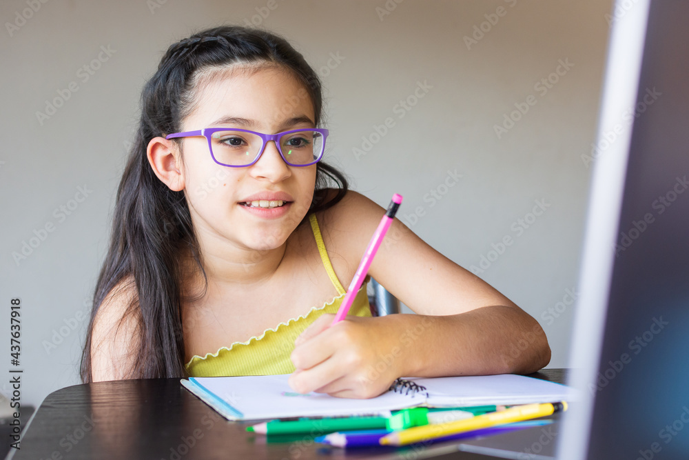 little girl doing homework with her notebook. Girl with glasses copying ...
