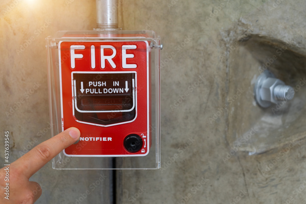 Finger to press at red fire alarm switch box on the raw concrete wall ...