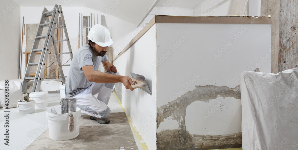man plasterer construction worker at work, takes plaster from bucket ...