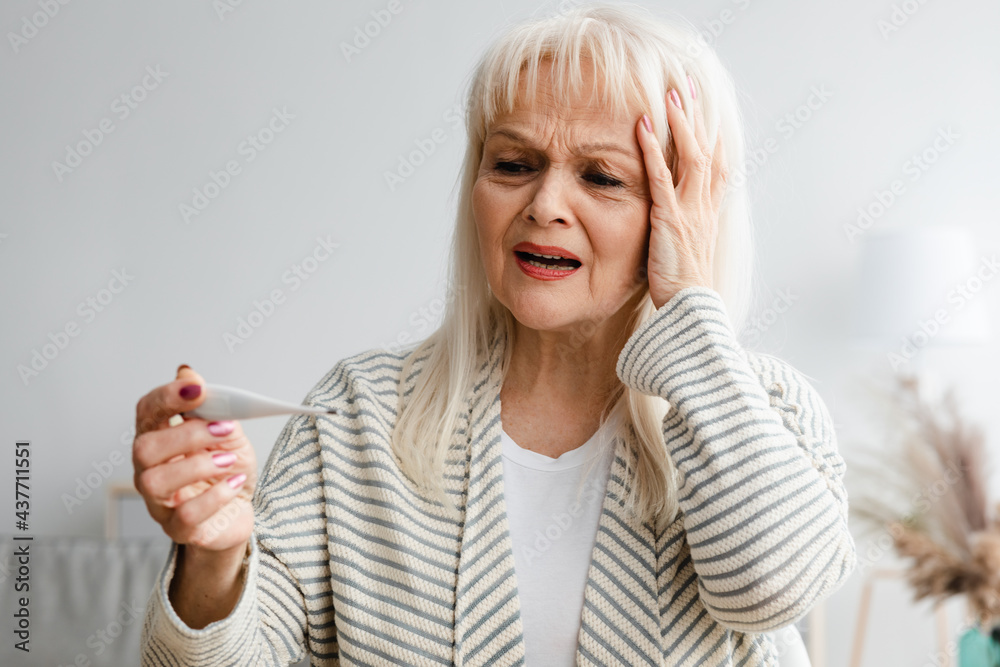 Scared mature lady checking body temperature looking at thermometer ...