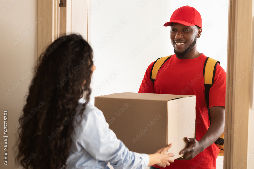 Black delivery man giving box to woman standing at door Stock Photo ...