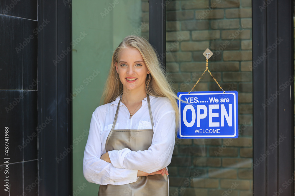 Beautiful blonde hair girl standing by open shop sign plate at door ...