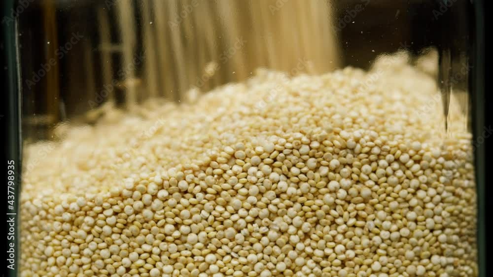 Close-up of falling down quinoa into glass jar on black background ...
