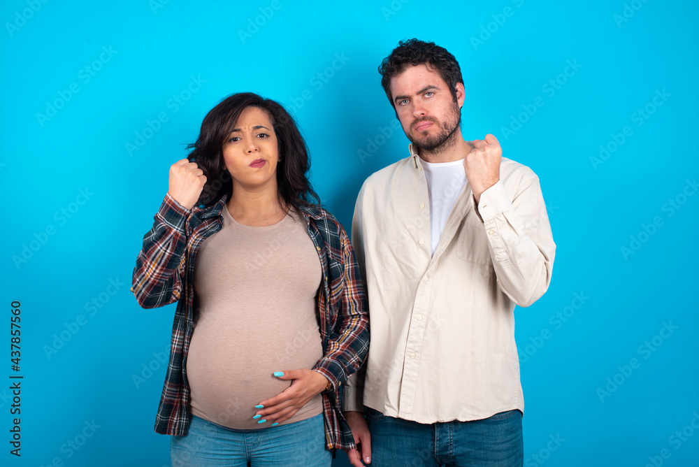 young couple expecting a baby standing against blue background shows ...