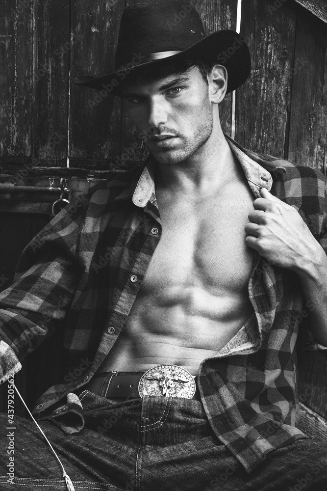 Handsome cowboy looking at camera wearing hat with open chequered shirt ...