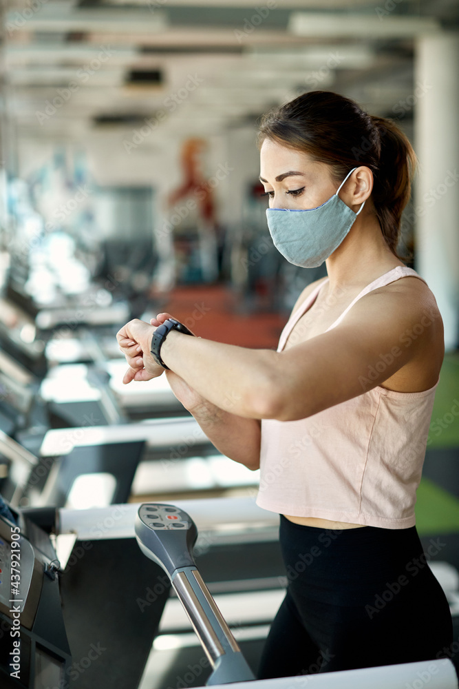 Athletic woman with face mask setting up her fitness tracker while ...
