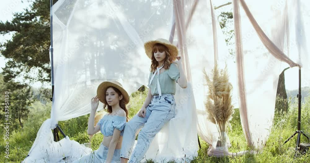 Two girls in straw hat and summer clothes posing on green field ...