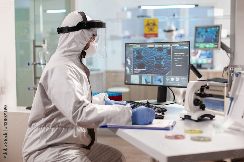Scientist in ppe suit taking notes on clipboard working on virus ...