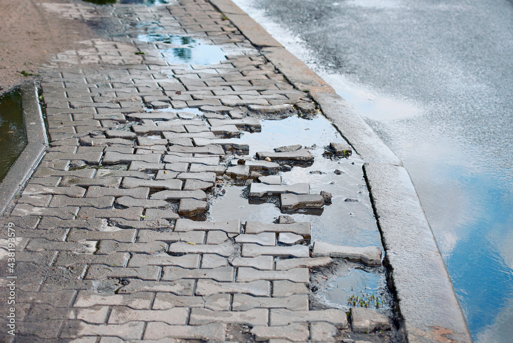 Puddle after rain on damaged paving slabs, dangerous pedestrian walkway ...