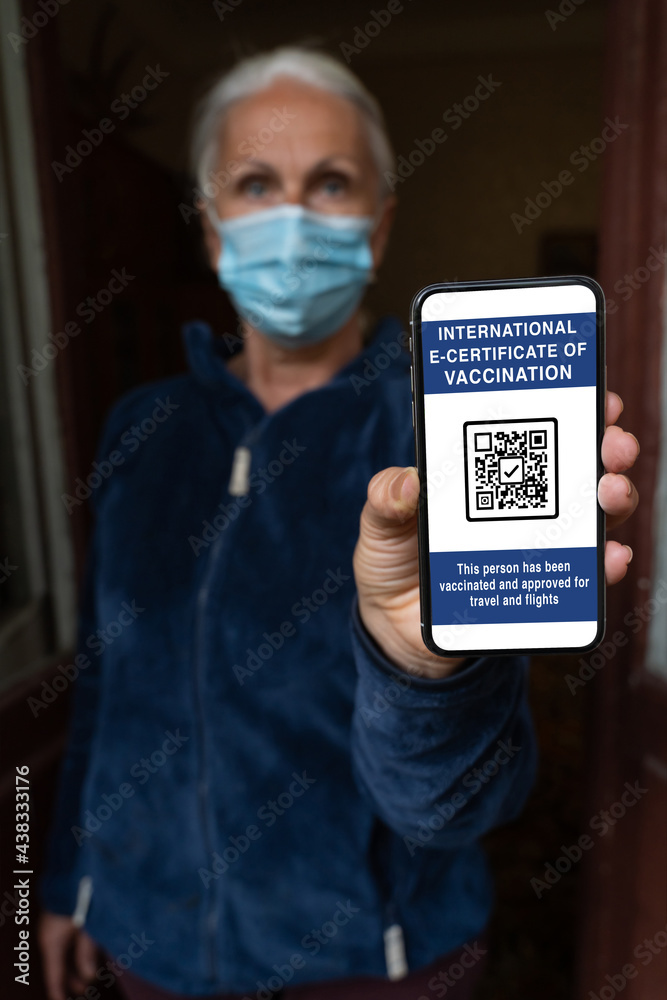 A middle-aged woman in mask is holding a smartphone with electronic ...
