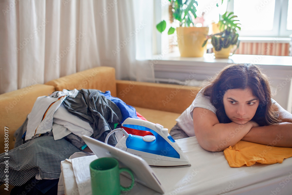 Tired middle aged woman watches video on tablet and ironing things at ...