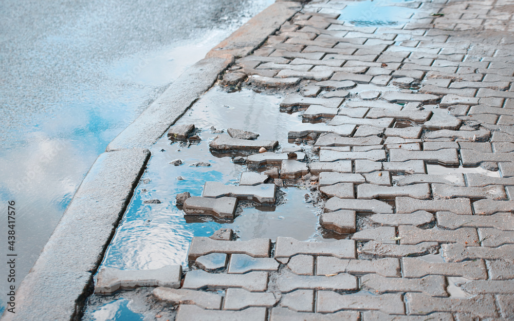 Puddle after rain on damaged paving slabs pedestrian walkway. Pit with ...