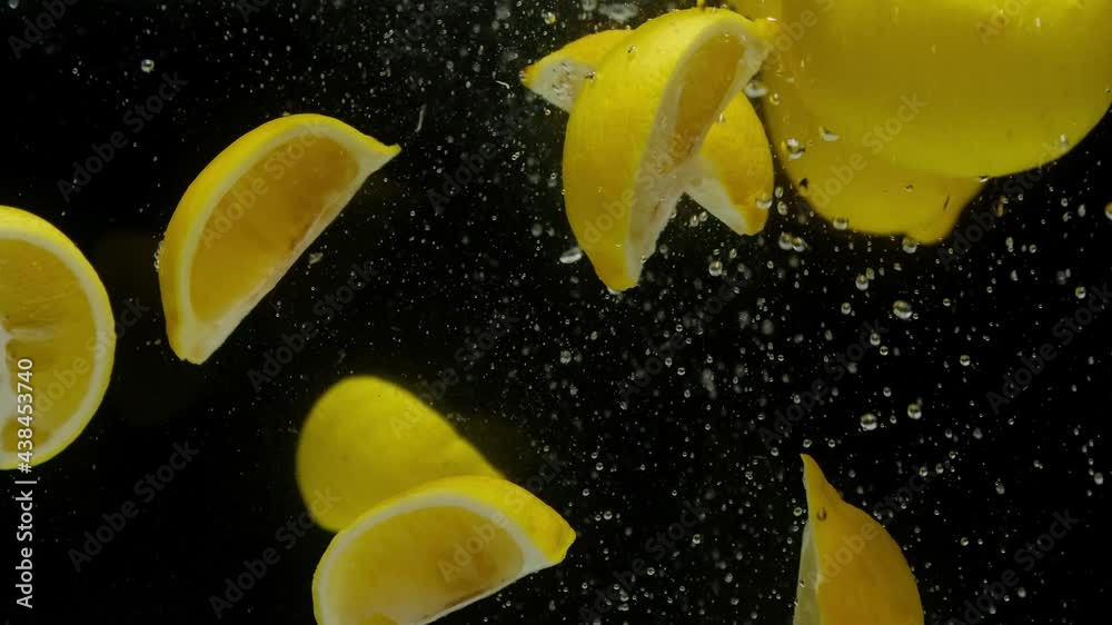 Close-up of falling sliced lemons into the sparkling water on black ...