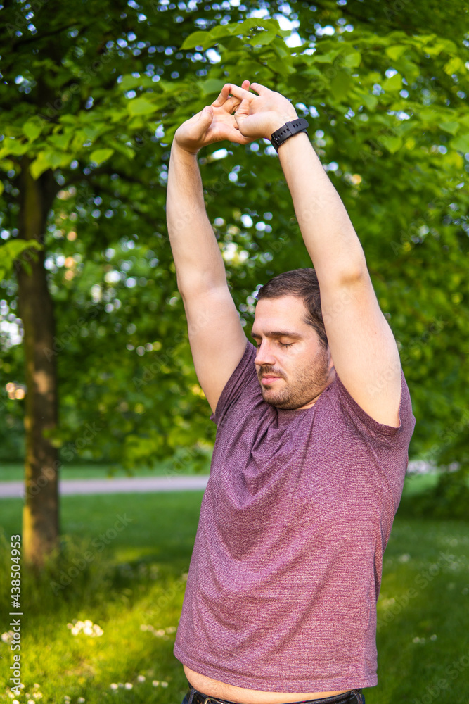 Photo of a young and attractive man in the park streching with his arms ...