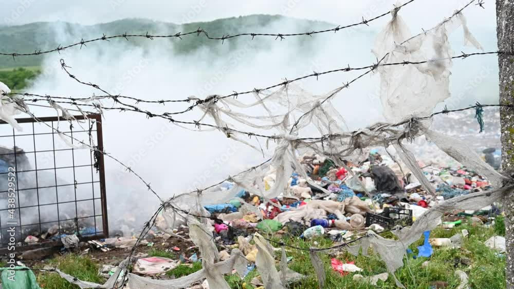 Barbed wire fence around open landfill site with burning waste. Burning ...