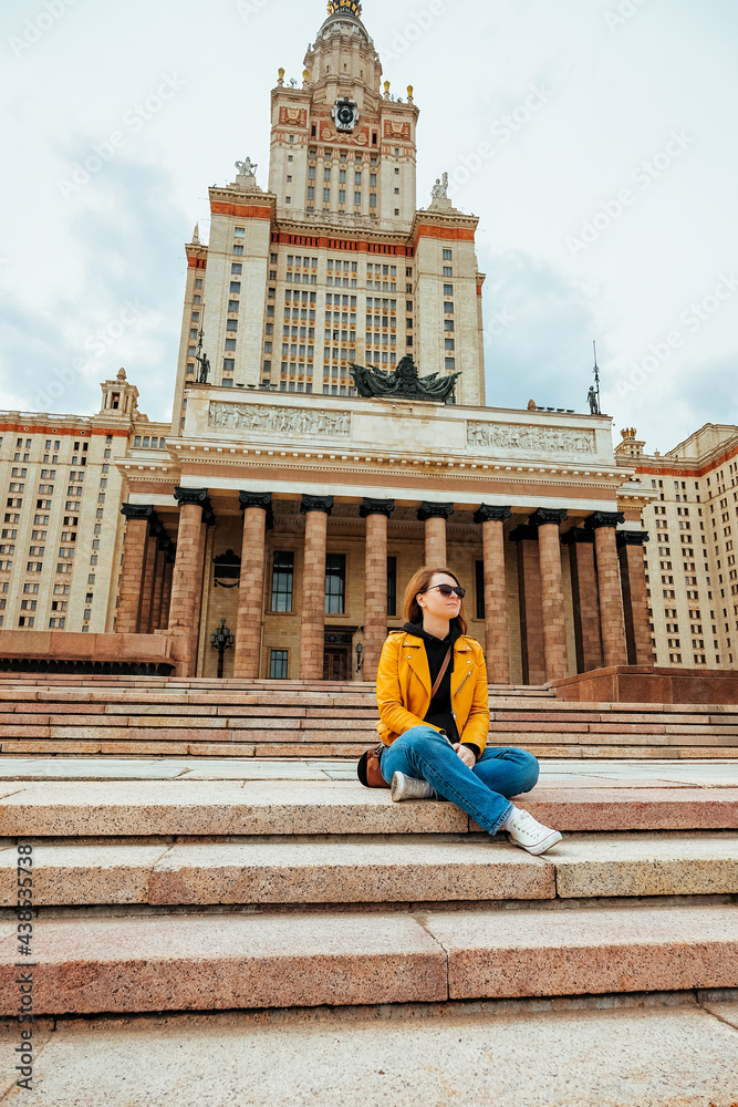 young female student in a yellow jacket, jeans and glasses sits on the ...