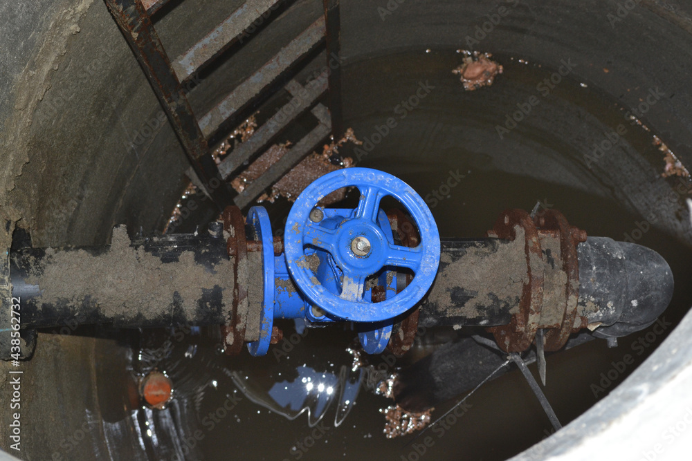 An open round hatch in a concrete block.A black pipe with a blue valve ...