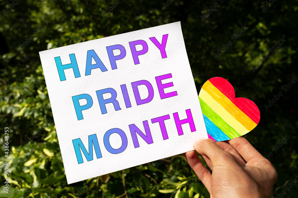 hand holds a poster with happy pride month title and the heart colored ...