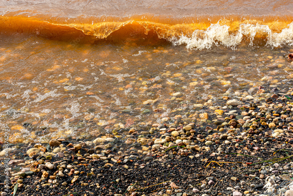 The shore of the reservoir is covered with pebbles. River wave of dirty ...