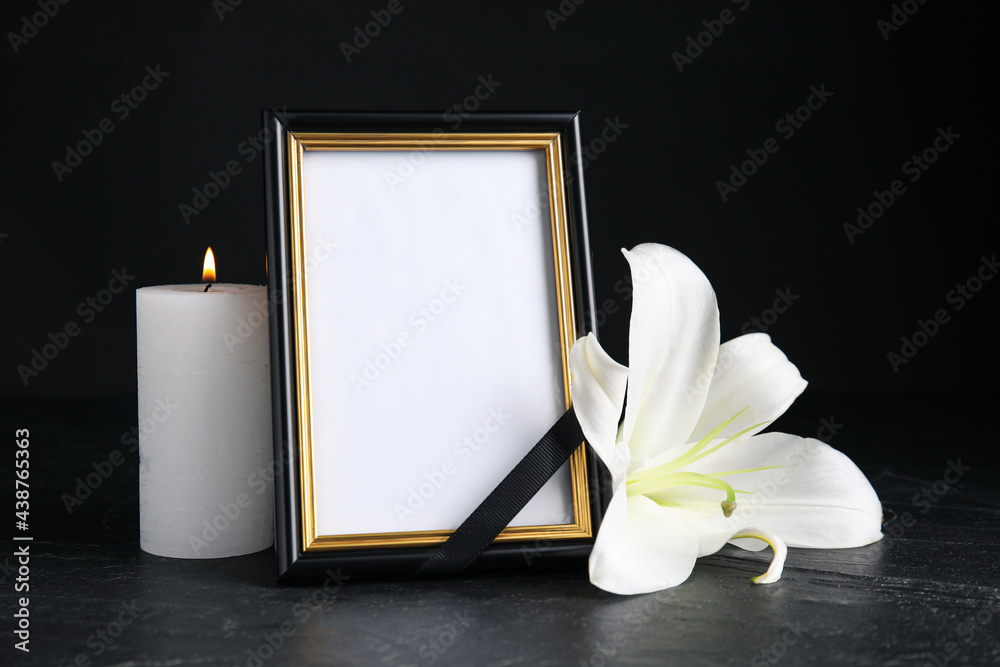 Funeral photo frame with ribbon, white lily and candle on black table ...