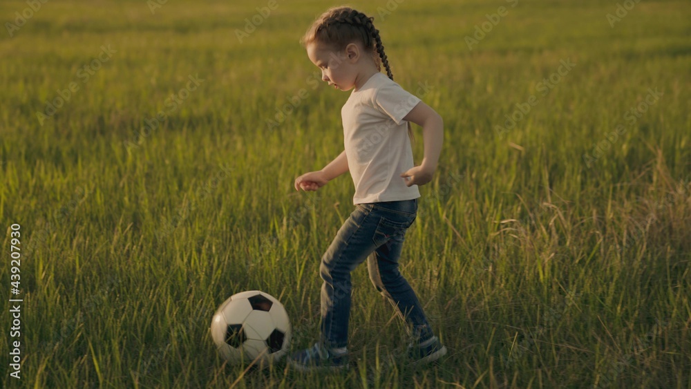 Little child runs across the green football field playing football at ...
