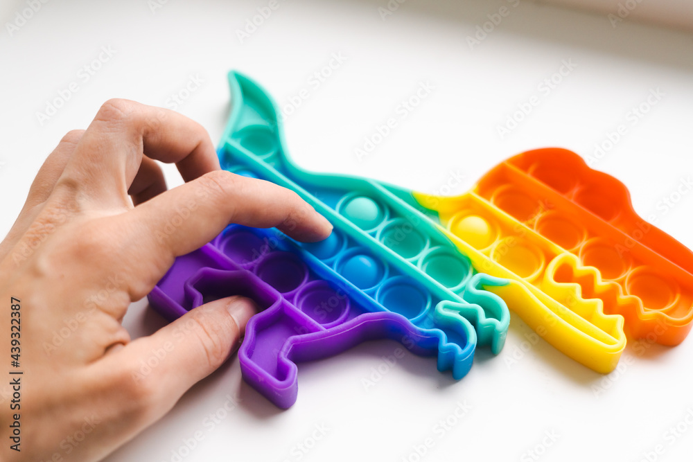 Popit rainbow toy in rainbow colours and dino shape. Trendy bubble pop ...