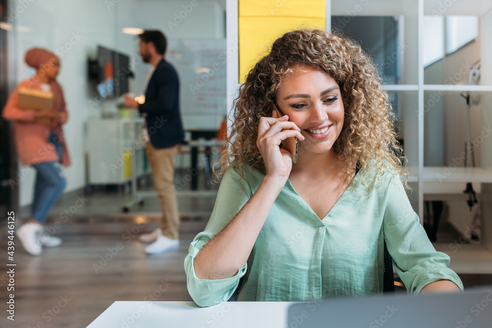 Smiling employee talking on smartphone against multiracial colleagues ...
