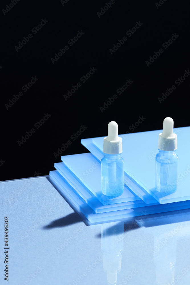 Small bottle of serum on stack of glass plate on color background ...