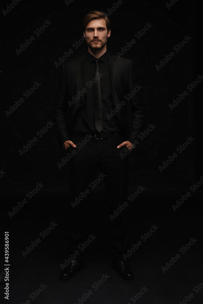 Young man in black suit full body portrait against black background ...