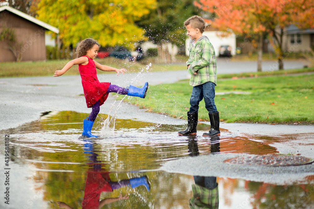 Girl kicks water from puddle at brother Stock Photo | Adobe Stock