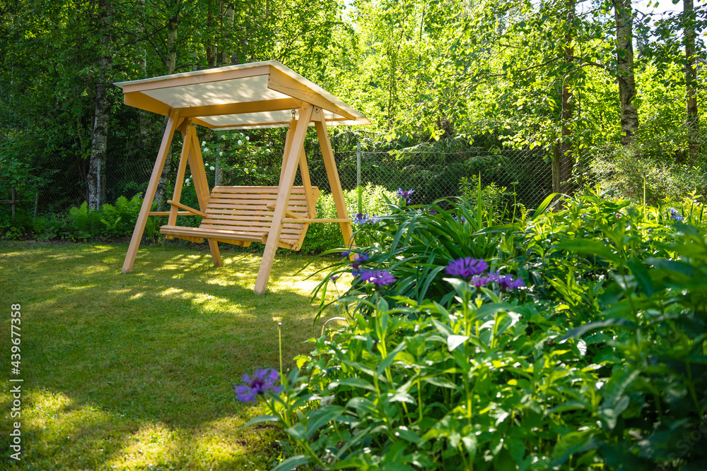 Wooden garden swing in a green garden in summer, relax in nature ...