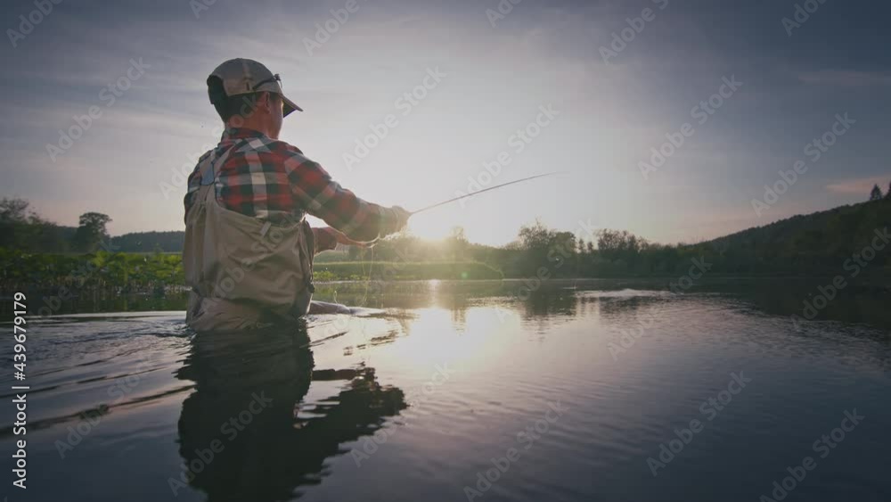 Fly fishing. Angler stands in the river and casts the fly at sunset ...