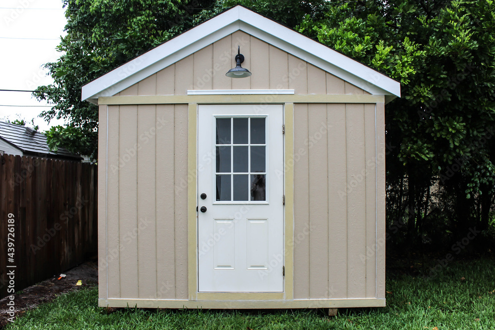 Front view of a backyard tool shed with a dog outside in a yard. Many ...