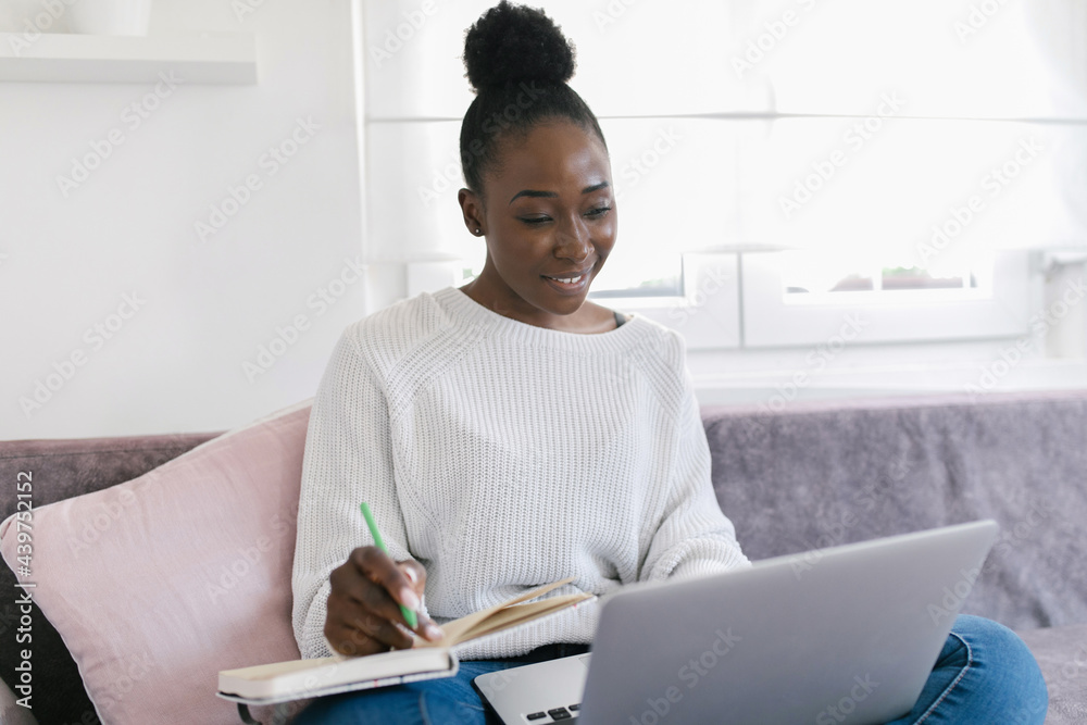 Young black woman studying from home, using her laptop and writing ...