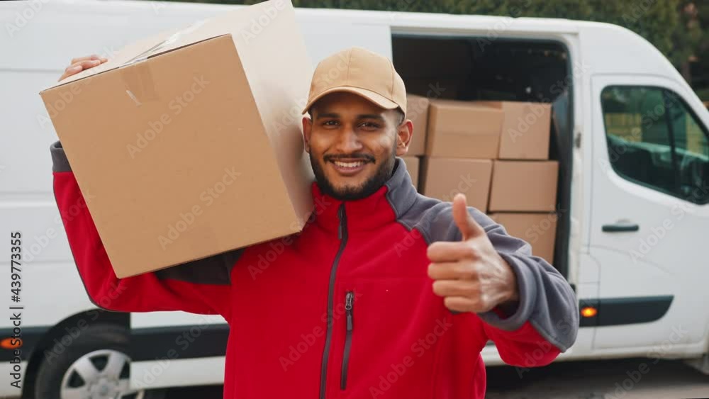 Delivery boy carrying a cardboard box on his shoulder. Smiling and ...