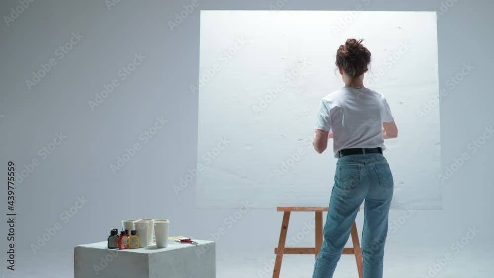 Back view, female artist applies a layer of white primer on a large ...