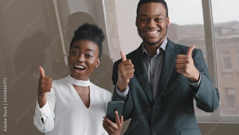 Emotional happy cheerful young African ethnic colleagues looking at ...
