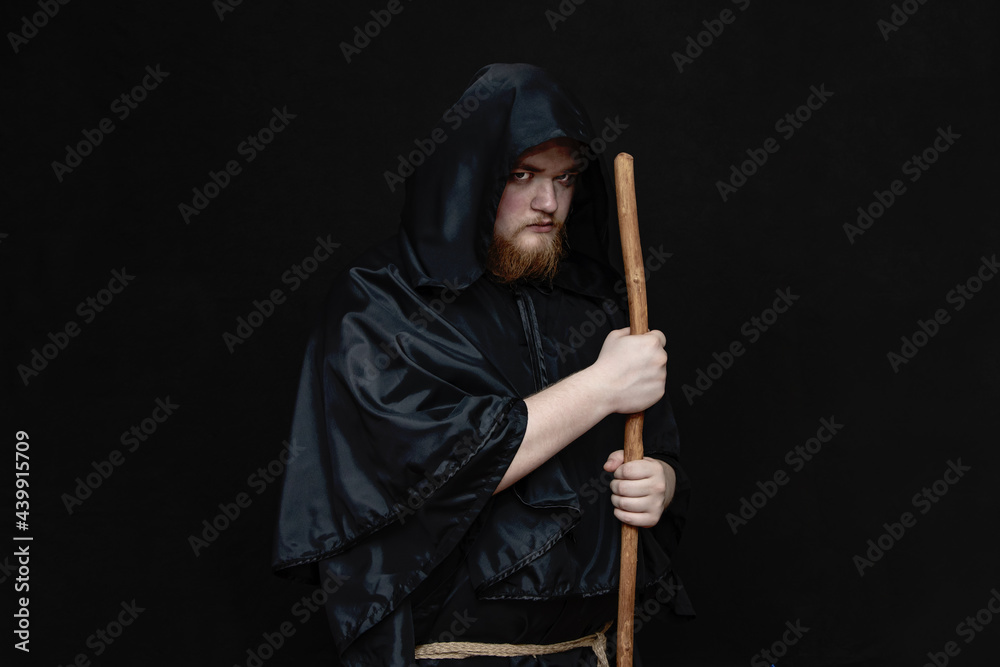 A monk in a black hood with a staff on a dark background, a gloomy ...