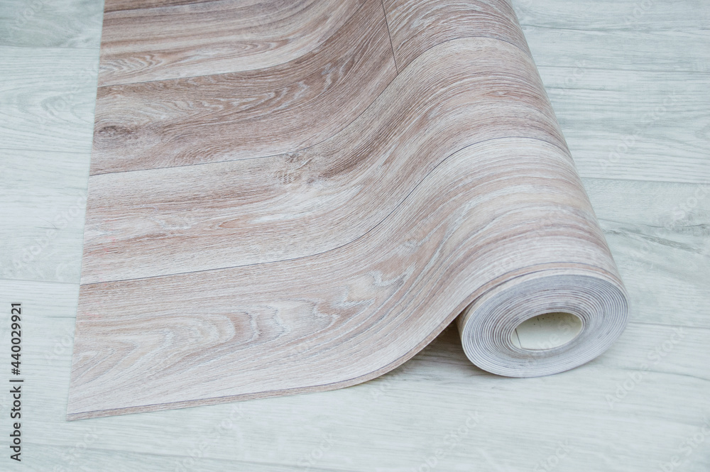 Unwound roll of beige linoleum with wood texture on white wooden floor ...