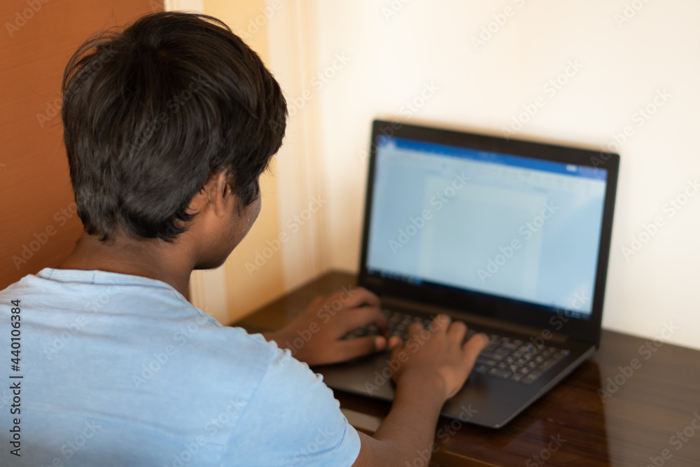 Portrait of a young Indian teen typing on laptop. Indian student uses ...