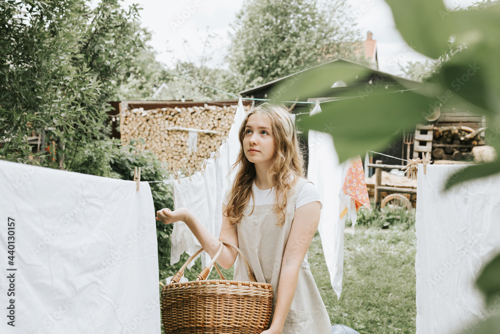blonde teen girl in linen apron is doing homework washing clothes in ...