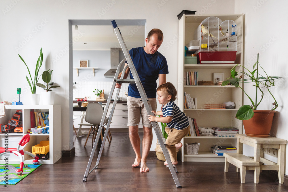 Cute toddler climbing ladder being held by father in playroom at home ...