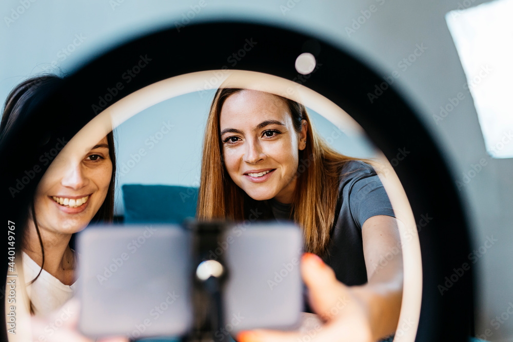 Smiling female influencers vlogging using mobile phone at home Stock ...