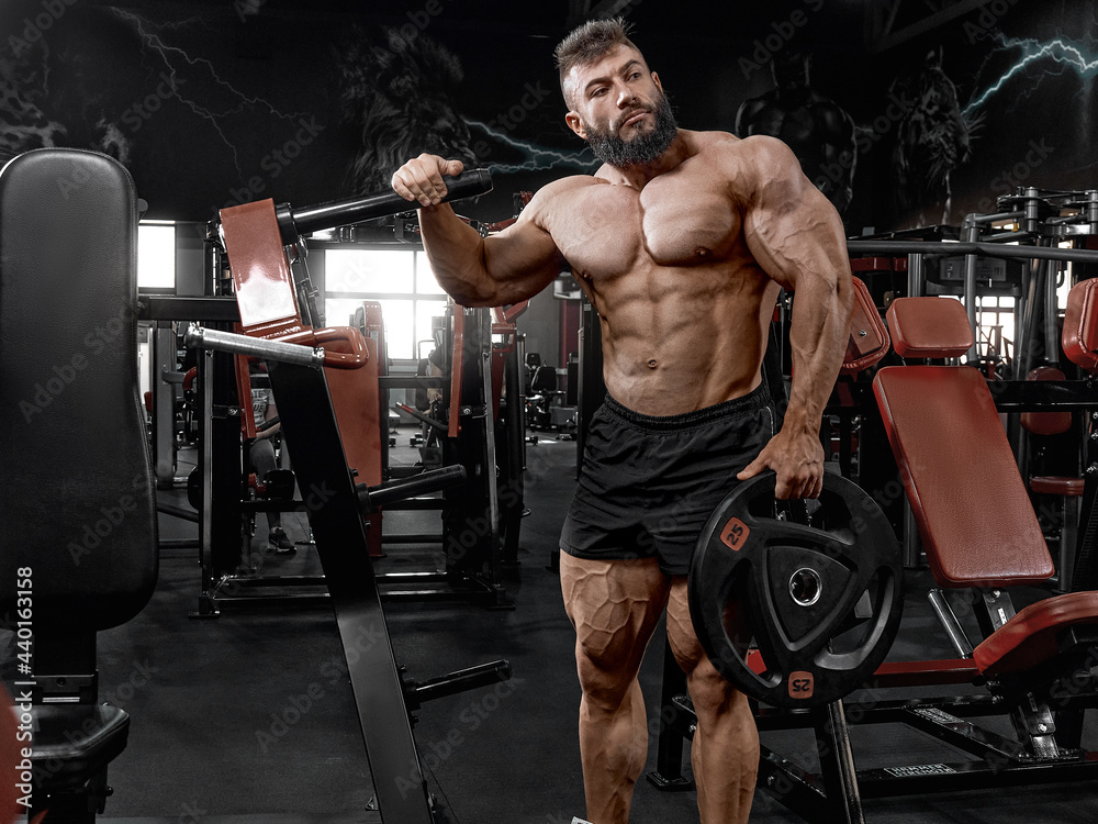 Brutal man with a beard holds a 25 kg disc in his hands in the gym. A ...