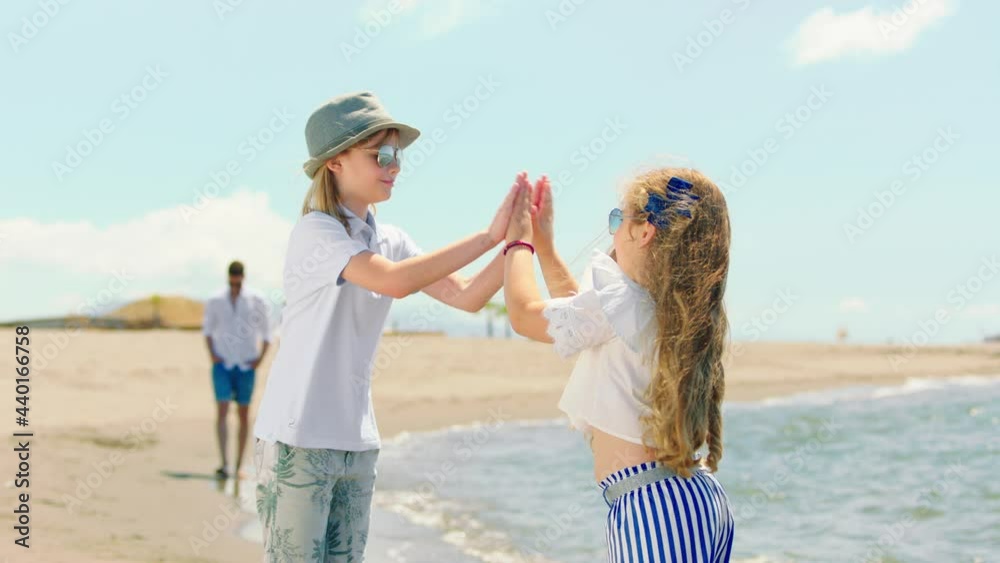 School age boy and girl playing clapping game at beach, standing at ...