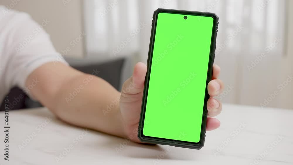Man's hand shows mobile smartphone with green screen in vertical ...