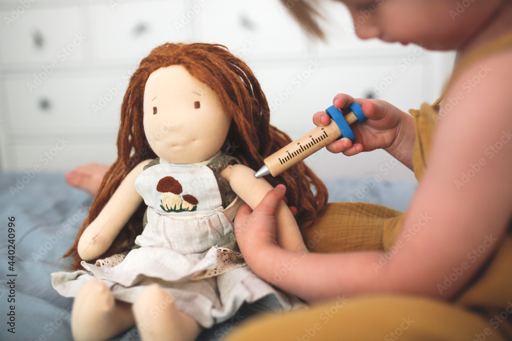 Girl child makes an injection with a wooden syringe to a doll on the ...
