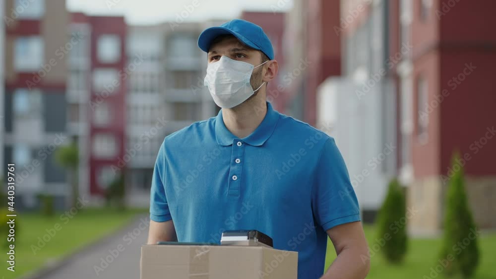 An young mailman courier with a protective mask and gloves is ...