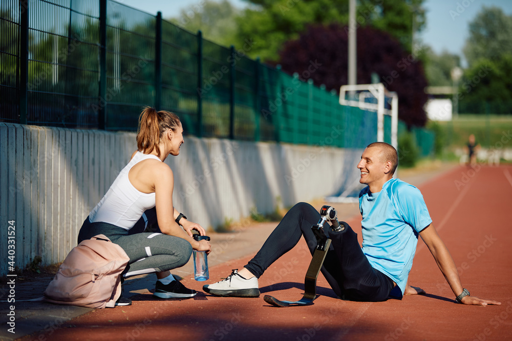 Happy disabled athlete and his female friend talking while relaxing on ...